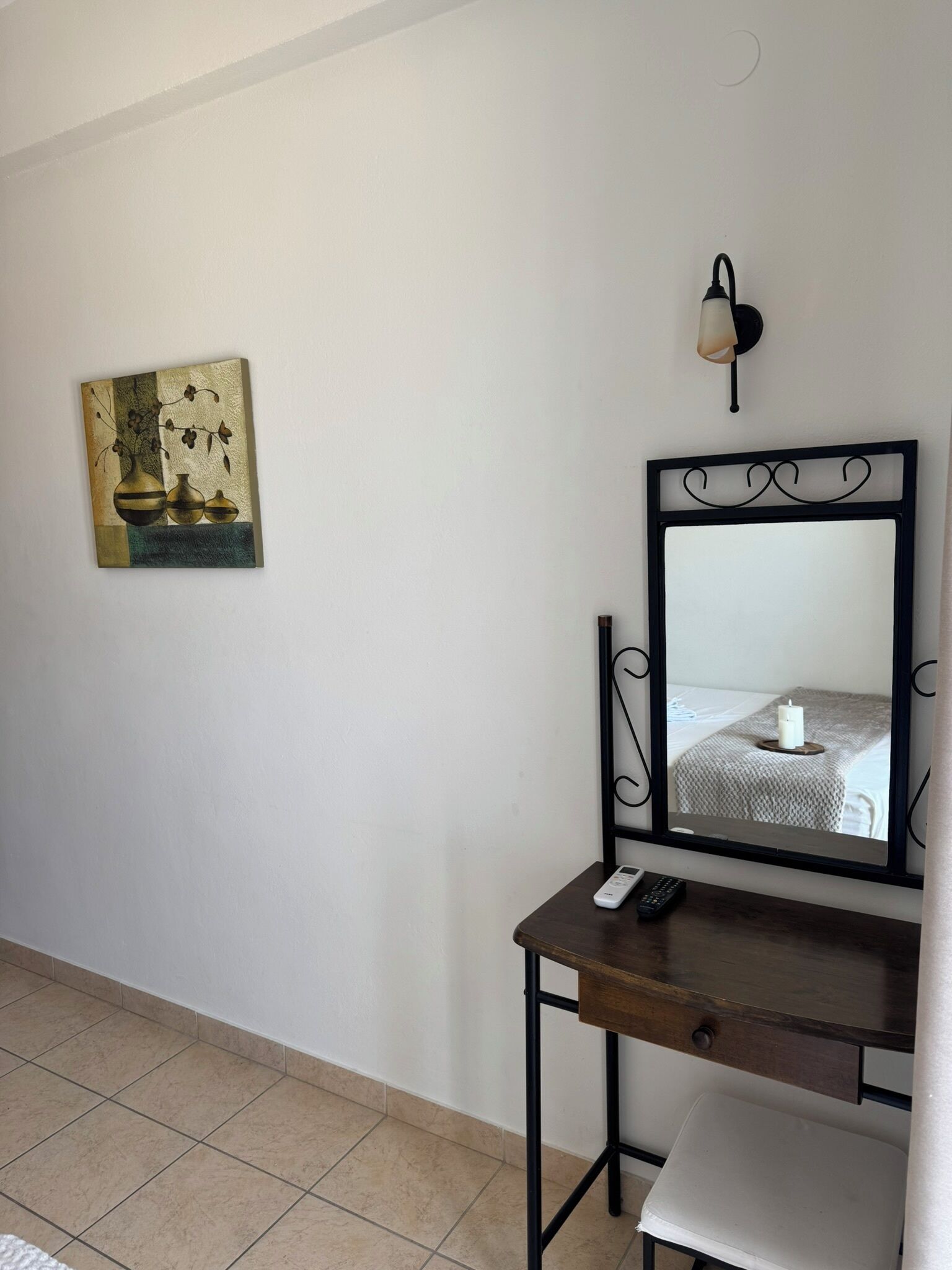 Quarto com escrivaninha, espelho, luminária na parede e um quadro.
