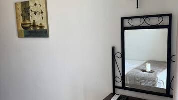 Quarto com escrivaninha, espelho, luminária na parede e um quadro.