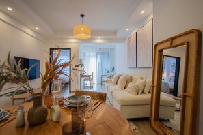 Uma sala de estar moderna com área de jantar, um sofá, um espelho grande e uma televisão.