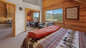 Interior de cabana de madeira com cama, dois sofás, lareira e um cartaz emoldurado sobre a vida selvagem.
