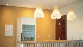 Uma área de recepção com balcão de madeira, uma geladeira abastecida com bebidas e três luminárias pendentes.