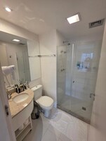 Uma casa de banho moderna com cabine de duche em vidro, sanita branca e toucador com lavatório.