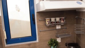Uma cozinha com porta azul, pia de aço inoxidável, armários brancos e um pequeno vaso com planta.