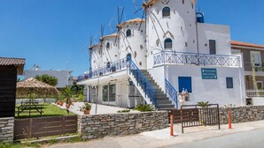 Um edifício branco com escadaria e guarda-corpo azul, uma pequena capela e uma placa indicando uma hospedaria em estilo moinho.