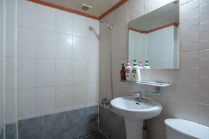 Casa de banho com chuveiro, pia, sanita e espelho com artigos de higiene pessoal.