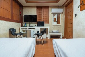 Quarto de hotel com duas camas, uma escrivaninha com computador, uma televisão e um guarda-roupa.