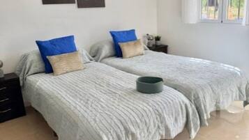 Quarto com duas camas, uma mesinha de cabeceira, janela com cortinas e espelho fixado na parede.