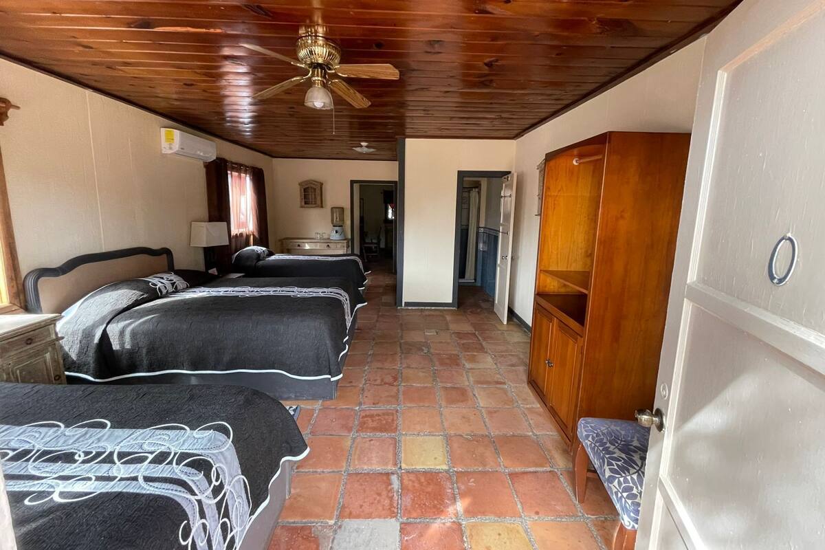 Quarto com três camas, teto de madeira, soalho em azulejos e porta com puxador.