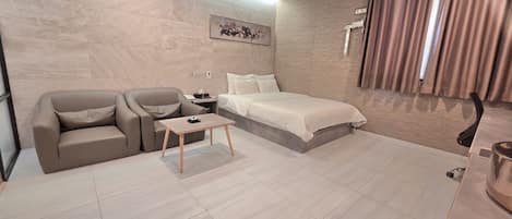 Quarto de hotel moderno com sofá, cama, mesa pequena e um quadro na parede.