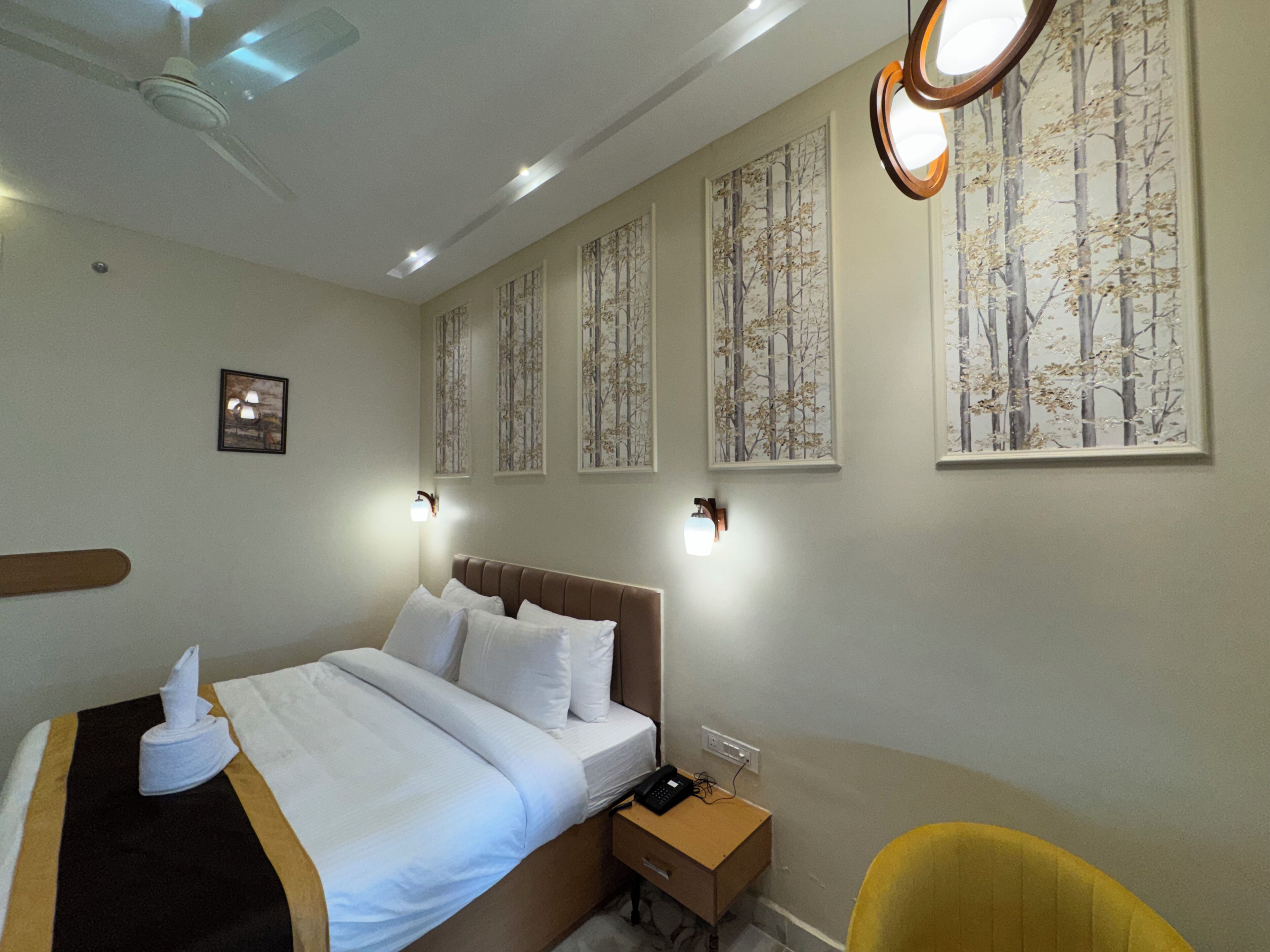 Quarto de hotel com cama, mesa de cabeceira, abajur e decoração na parede.