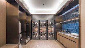 Uma lavanderia moderna com três máquinas de lavar empilhadas, um banco e um porta-toalhas.