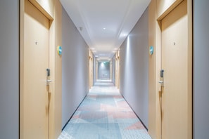Corredor de hotel com portas de madeira, carpete estampado e teto com iluminação embutida.