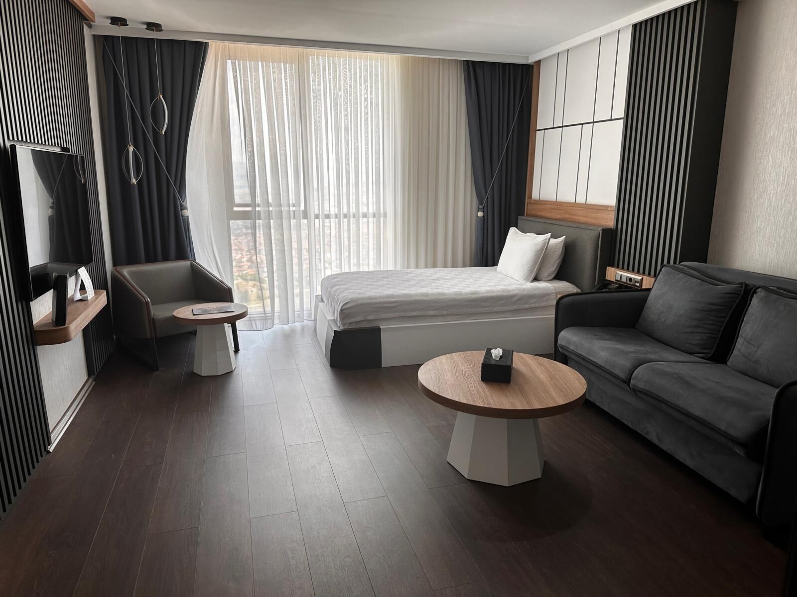 Quarto de hotel moderno com uma cama, um sofá, uma mesinha e uma televisão.