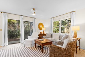 Um quarto com ventilador de teto, sofá, mesa de centro, cadeira de vime e abajur.