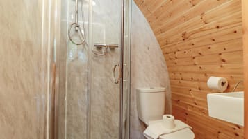 Um banheiro com box de vidro, vaso sanitário e painéis de madeira nas paredes.