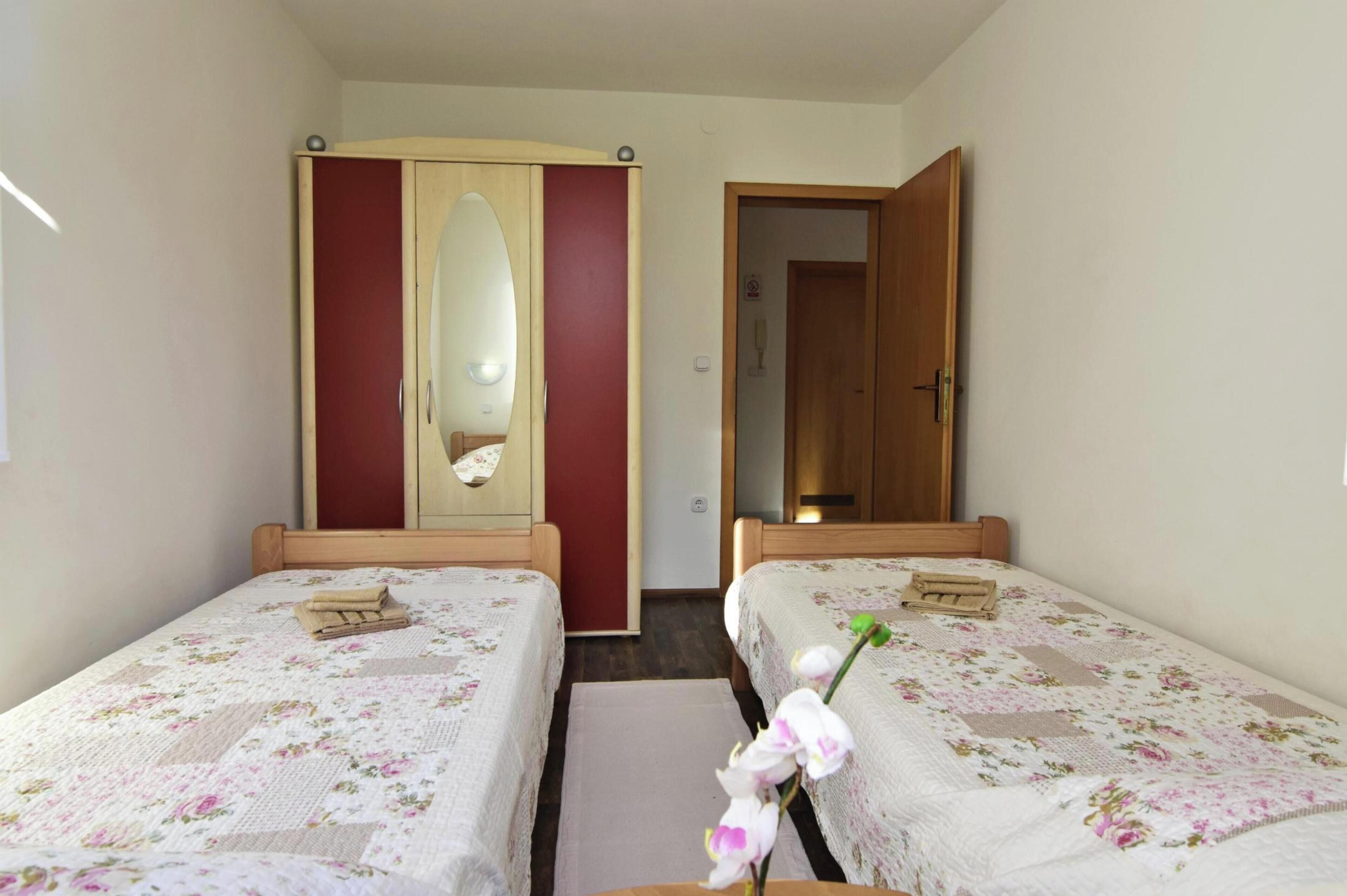 Quarto com duas camas de solteiro, um guarda-roupa e um espelho.