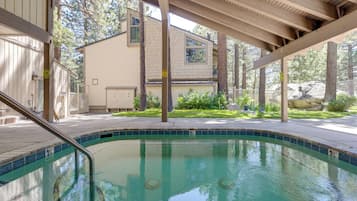 Uma piscina com borda azulejada, um deck de madeira e um edifício com fachada em azulejos ao fundo.