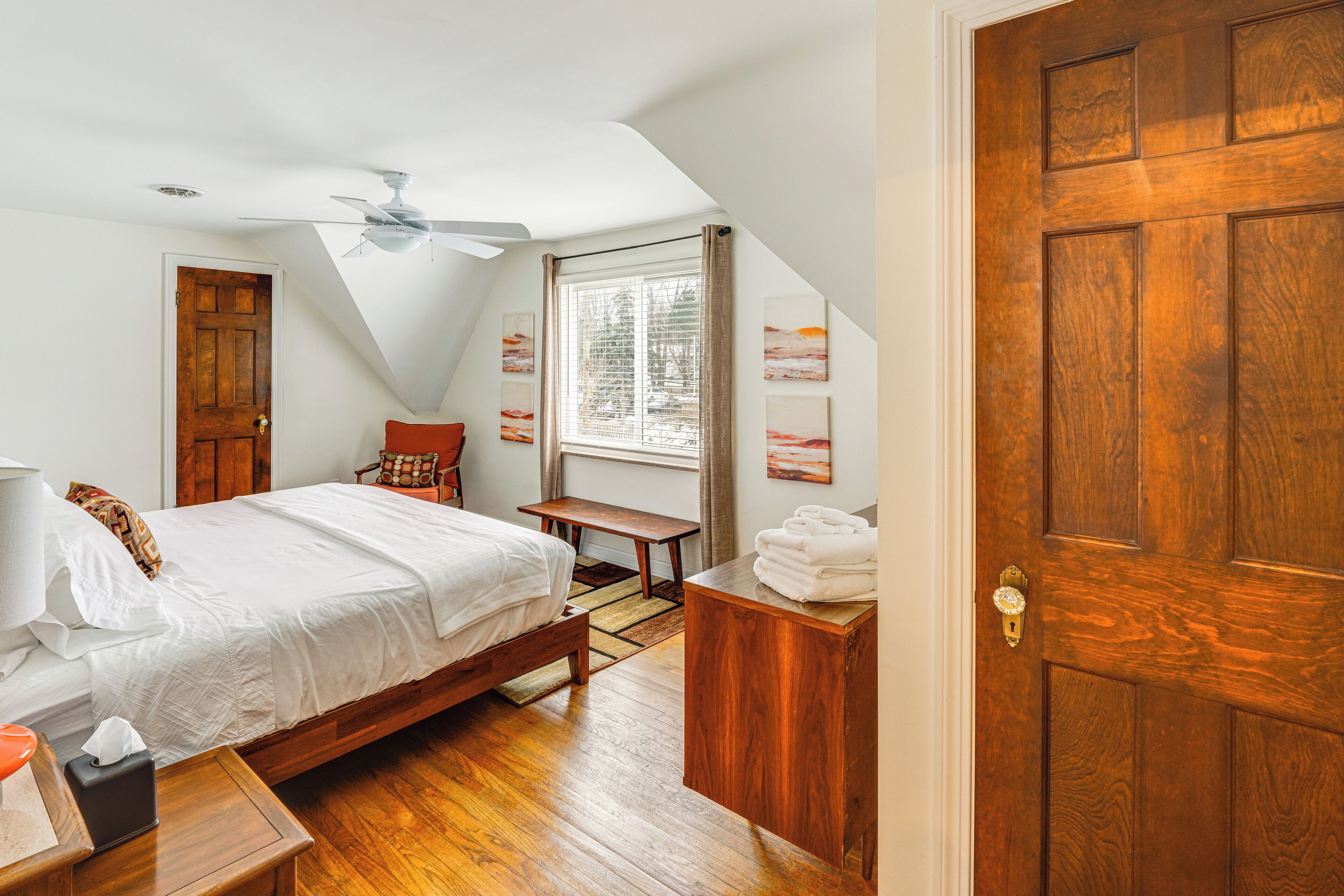 Quarto com cama de madeira, escrivaninha, cadeira e janela com cortinas.