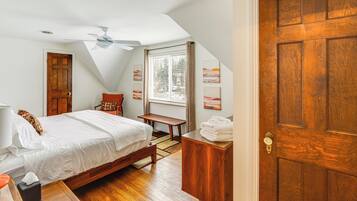 Quarto com cama de madeira, escrivaninha, cadeira e janela com cortinas.