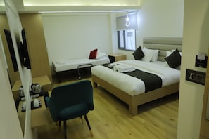 Quarto de hotel com cama, escrivaninha com cadeira, televisão e janela.