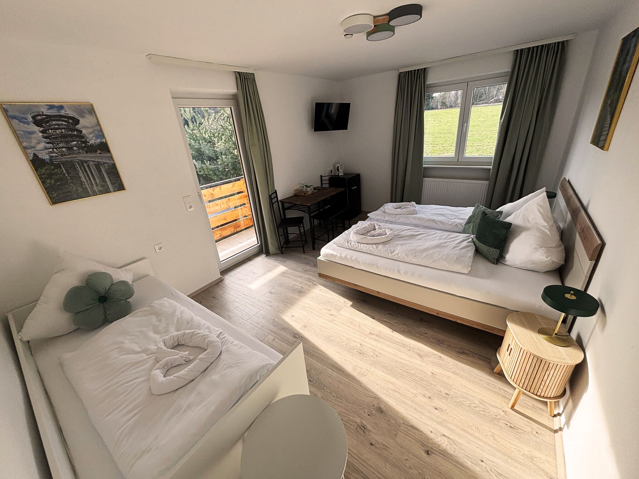 Quarto com duas camas, uma escrivaninha, televisão e varanda com vista para o verde.