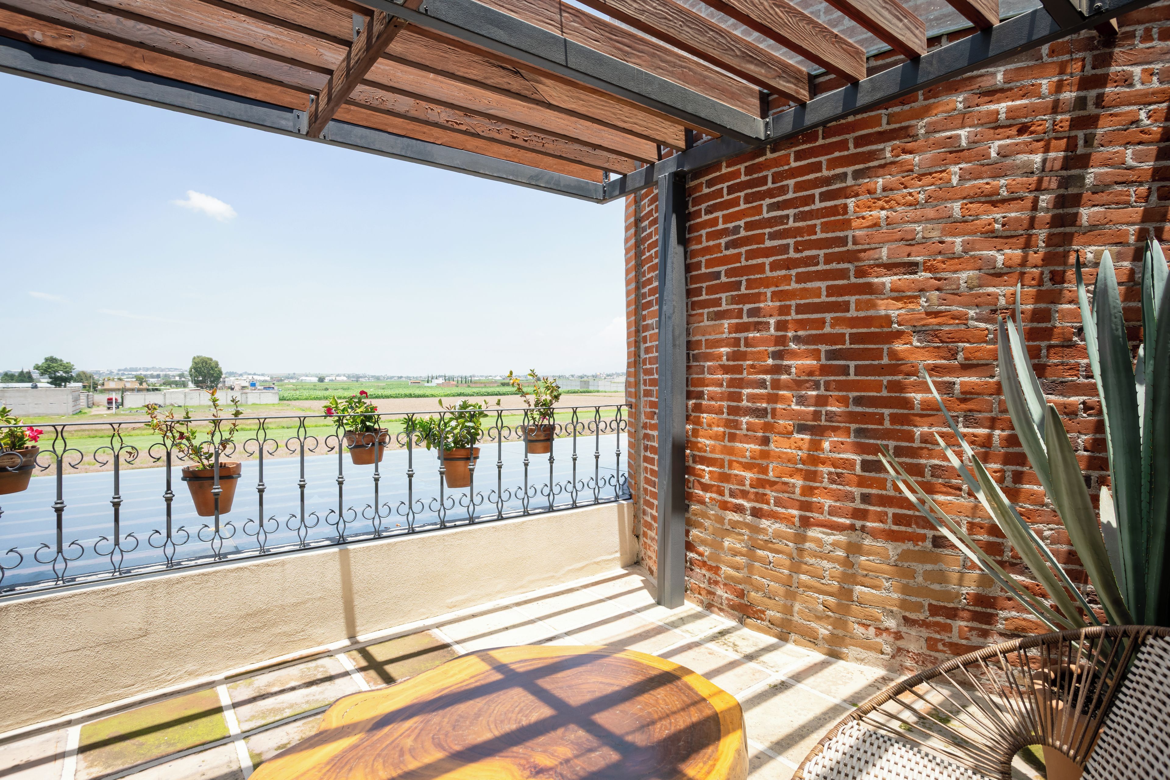 Varanda com vista para uma parede de tijolos, plantas em vasos e uma mesa de madeira.