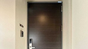 Uma porta metálica moderna com fechadura eletrônica, uma pequena placa acima dela e piso coberto de carpete.