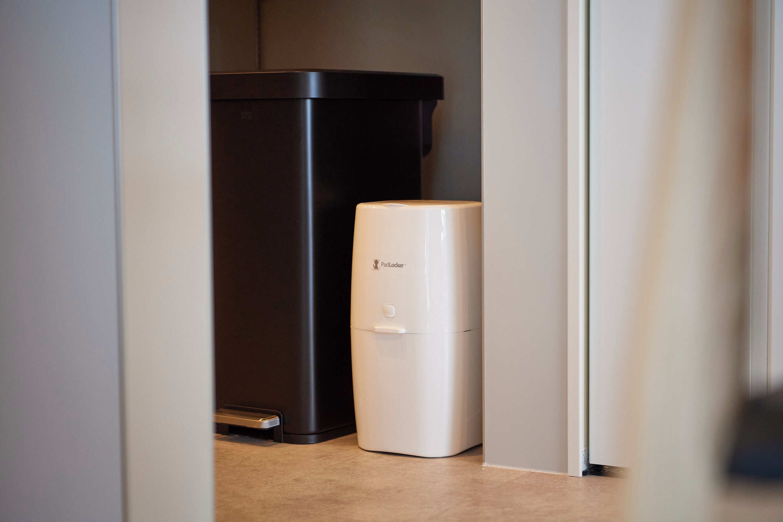 Uma lixeira compacta e um eletrodoméstico branco, provavelmente uma máquina de café, em um corredor estreito.