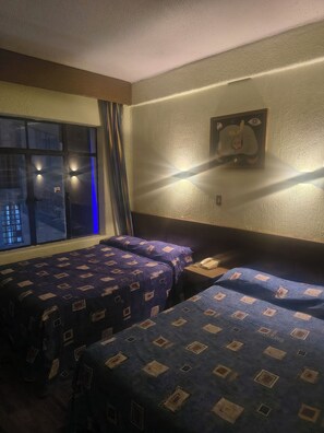 Quarto de hotel com duas camas, janela com cortinas, quadro pendurado na parede e telefone ao lado da cama.