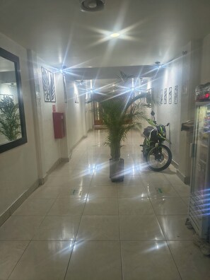 Um corredor com uma planta em vaso, uma motocicleta e uma máquina de vendas.
