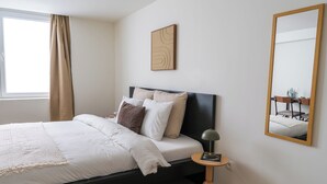 Um quarto com cama, mesa de cabeceira, abajur e um espelho na parede.