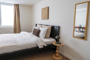 Um quarto com cama, mesa de cabeceira, abajur e um espelho na parede.