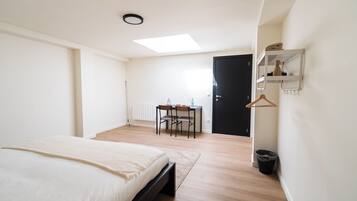 Quarto com cama, escrivaninha, cadeiras, porta preta e radiador.