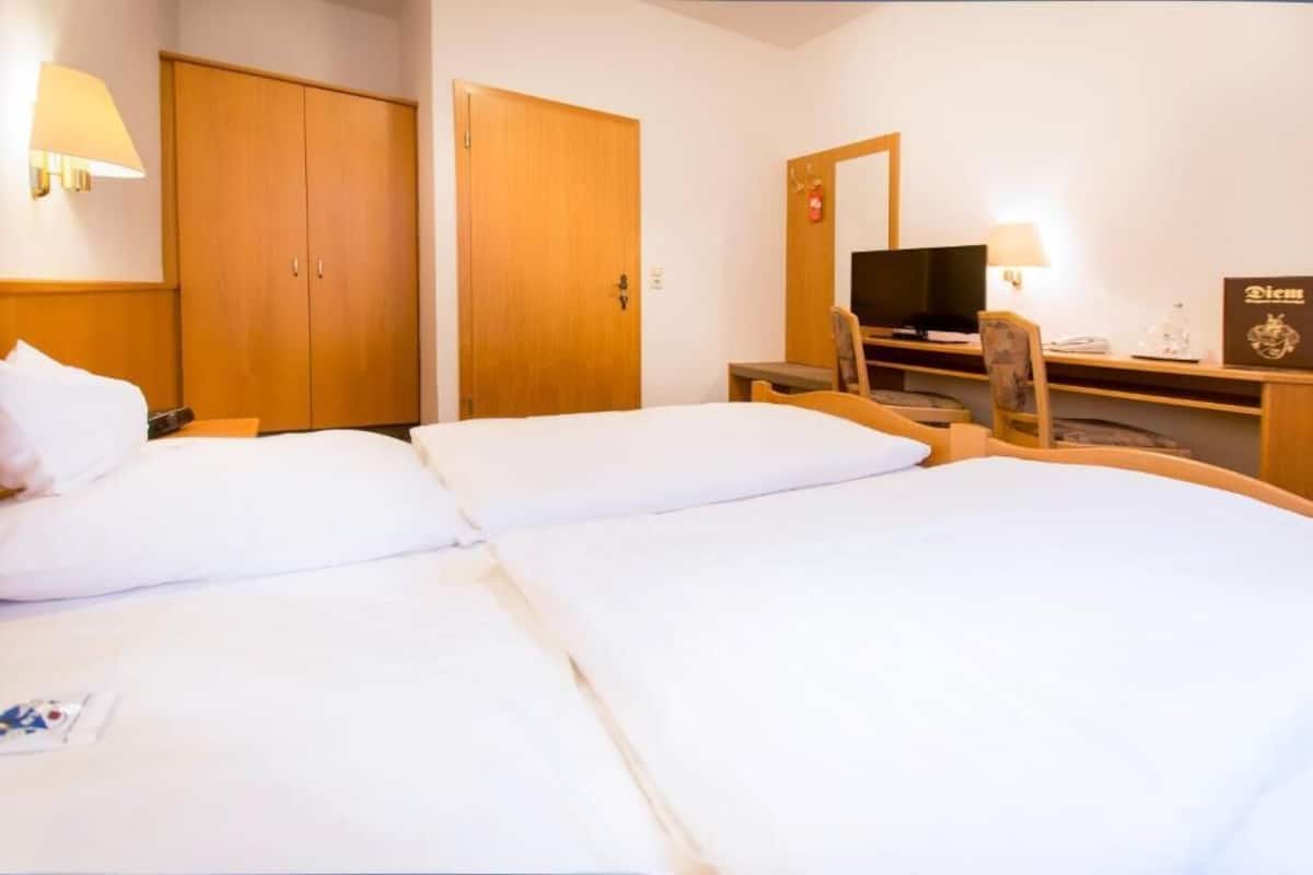Quarto de hotel com duas camas, uma mesa de escritório com computador, televisão e guarda-roupa.