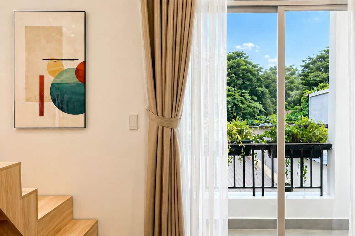 Quarto com escada, porta de vidro deslizante com cortinas e uma pintura abstrata emoldurada na parede.