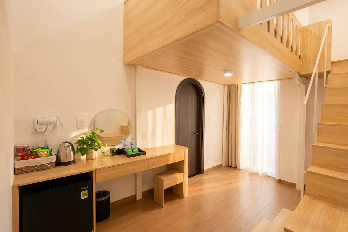 Quarto de hotel moderno com escrivaninha de madeira, kitchenette compacta, mini-geladeira, espelho e escada.