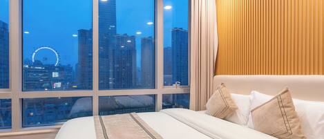 Quarto de hotel com uma grande janela, cama com roupa de cama branca e vista para a paisagem urbana, incluindo uma roda gigante.