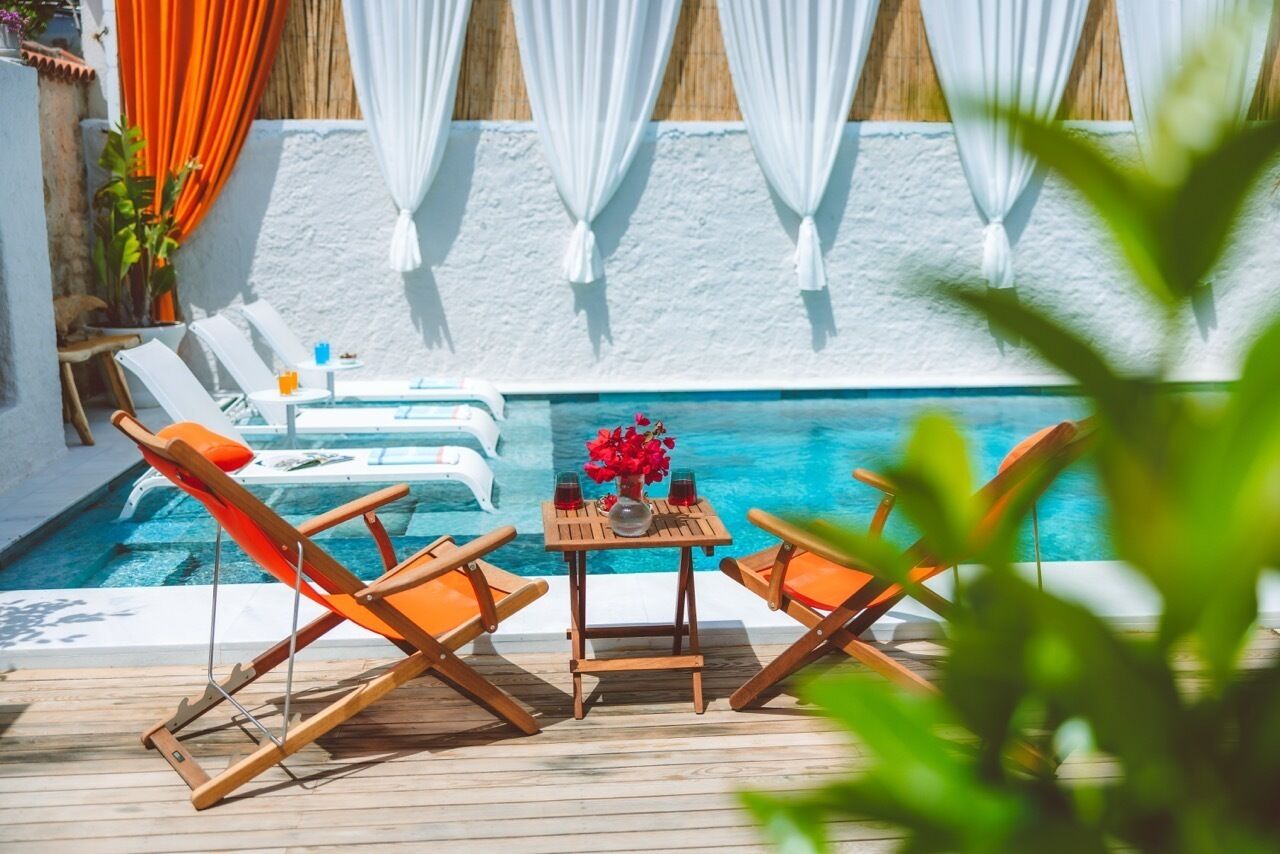 Uma área à beira da piscina com deck de madeira, espreguiçadeiras, uma mesa com um vaso de flores e a piscina.