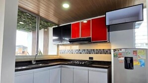 Cozinha moderna com armários brancos, geladeira de aço inoxidável e painel de proteção preto e vermelho.