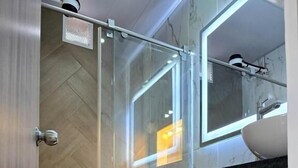 Casa de banho moderna com cabine de chuveiro em vidro, sanita branca e toucador com espelho.