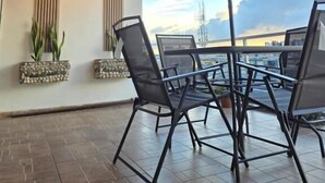 Uma área de estar externa com mesa e cadeiras, um grande guarda-sol e vista para o horizonte da cidade.