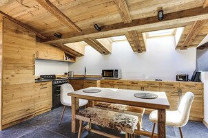 Interior em madeira com mesa de jantar, cadeiras, um banco e uma área de cozinha com eletrodomésticos.