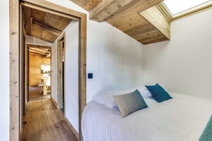 Quarto com claraboia, vigas de madeira, cama com almofadas e vista para uma sala de jantar.