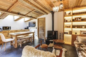 Uma sala de estar aconchegante com teto de madeira, lareira, estante de livros e um espaço de jantar com mesa e cadeiras.