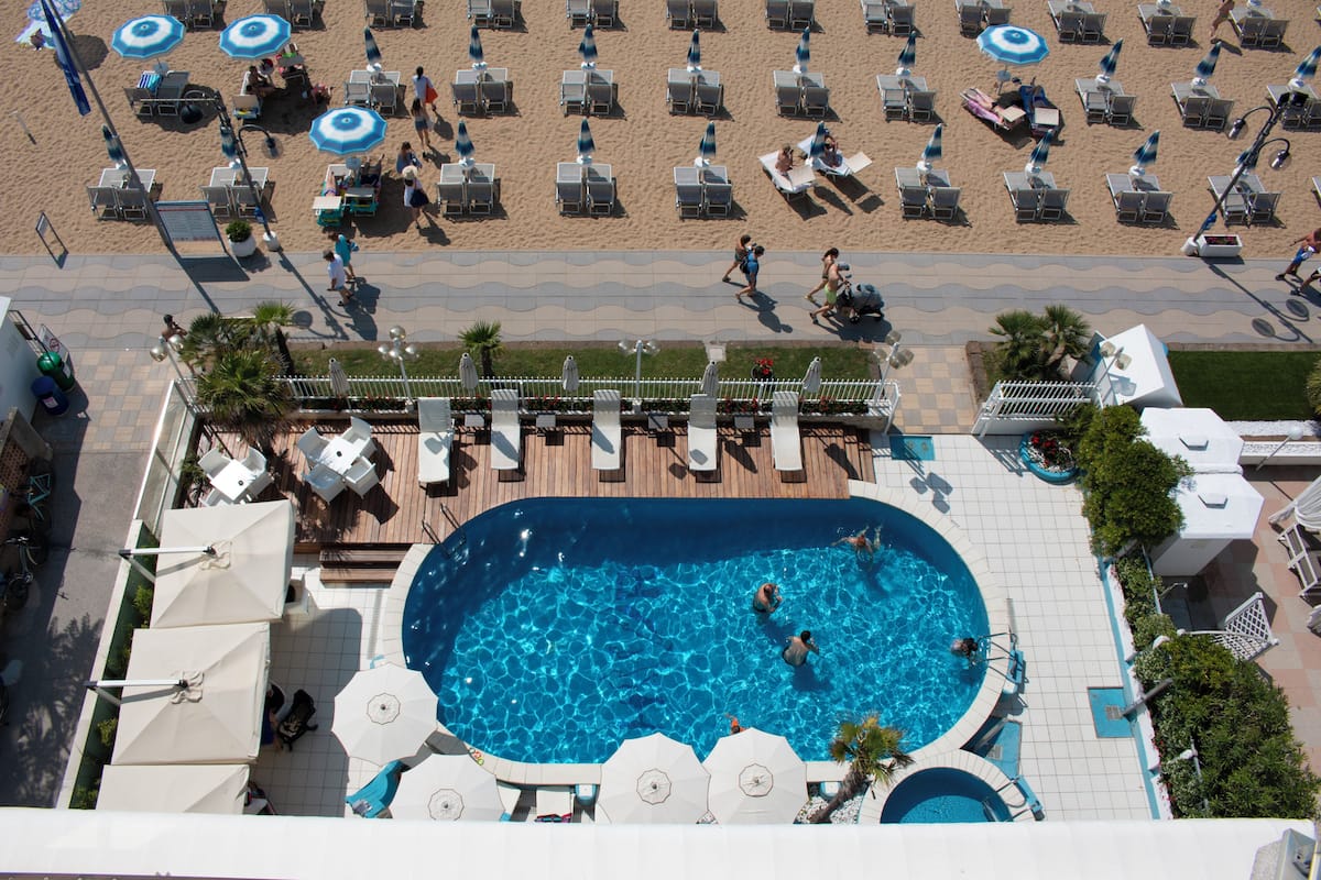 Piscina no terraço com espreguiçadeiras e guarda-sóis, rodeada por uma área de deck com poltronas de descanso e um bar à beira da piscina.