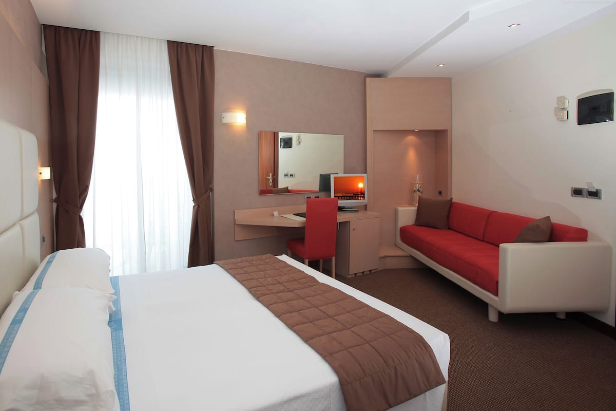 Quarto de hotel com cama, escrivaninha, cadeira e sofá vermelho.
