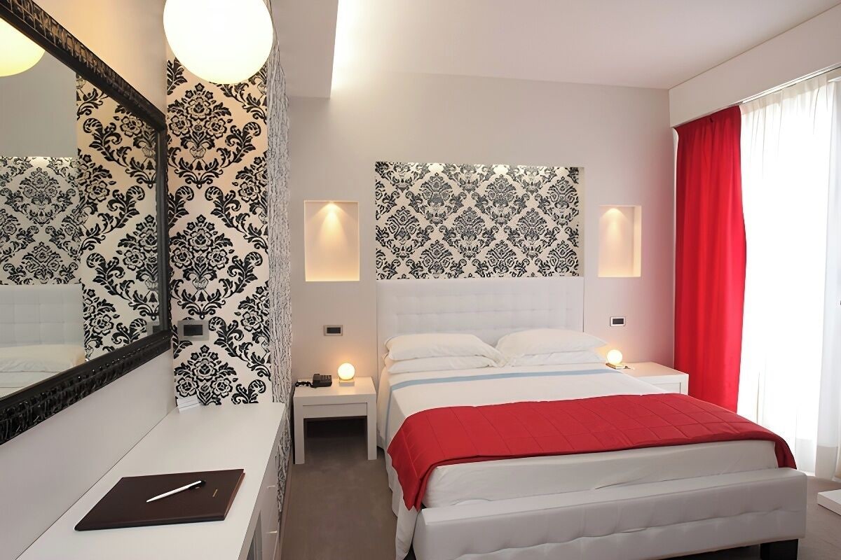 Quarto de hotel com cama, mesas de cabeceira, um espelho e papel de parede estampado.