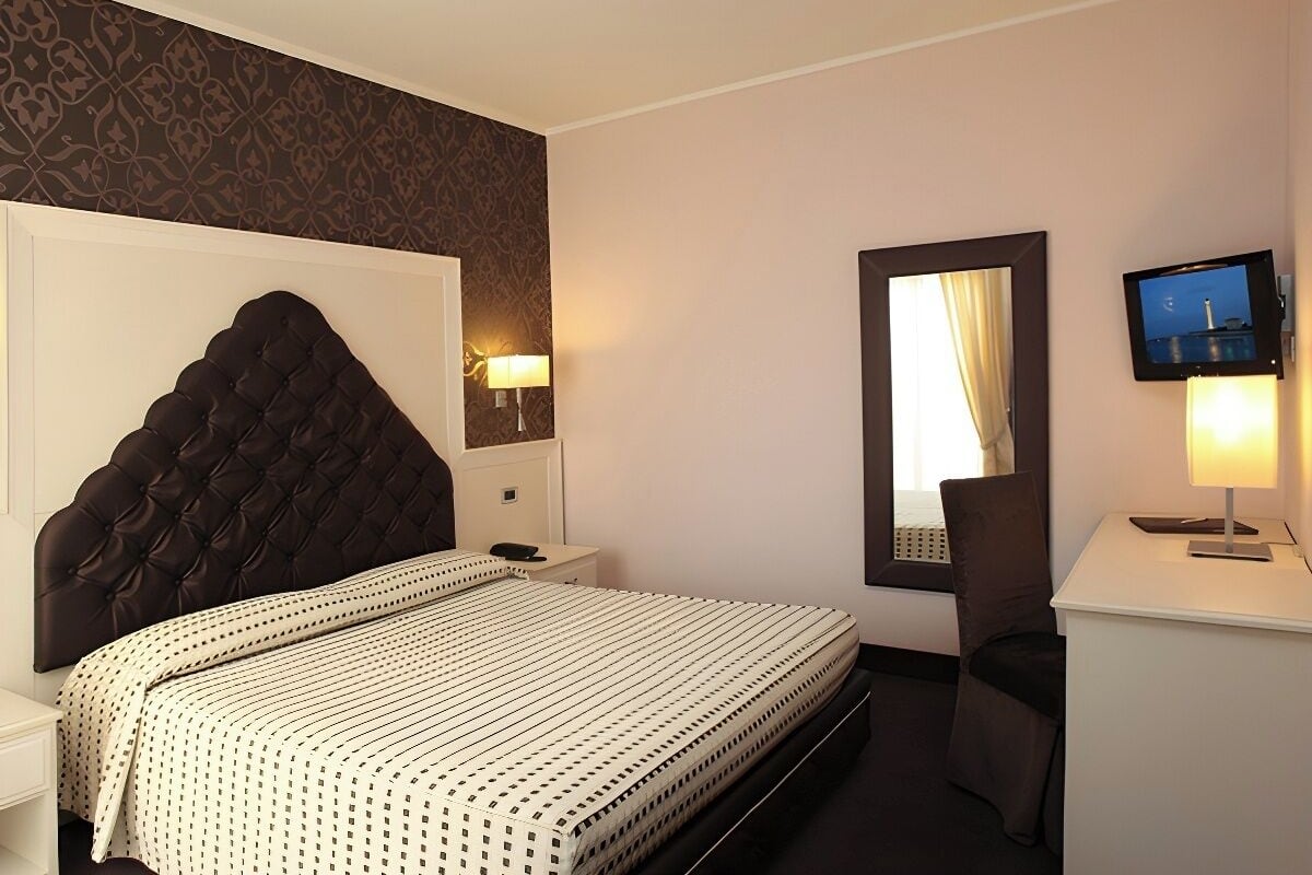 Quarto de hotel com uma cama grande, uma escrivaninha, uma cadeira, uma televisão e um espelho.