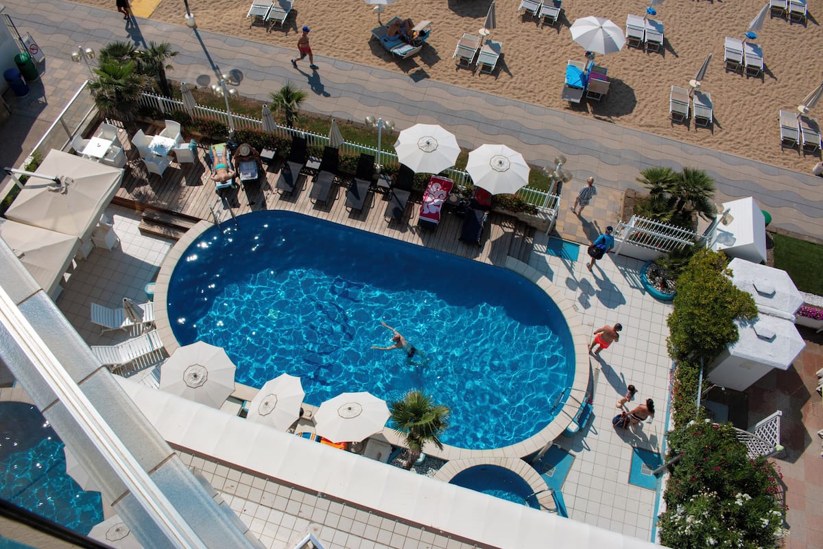 Piscina no terraço com vista para a praia, cadeiras de sol, guarda-sóis e posto de salva-vidas.
