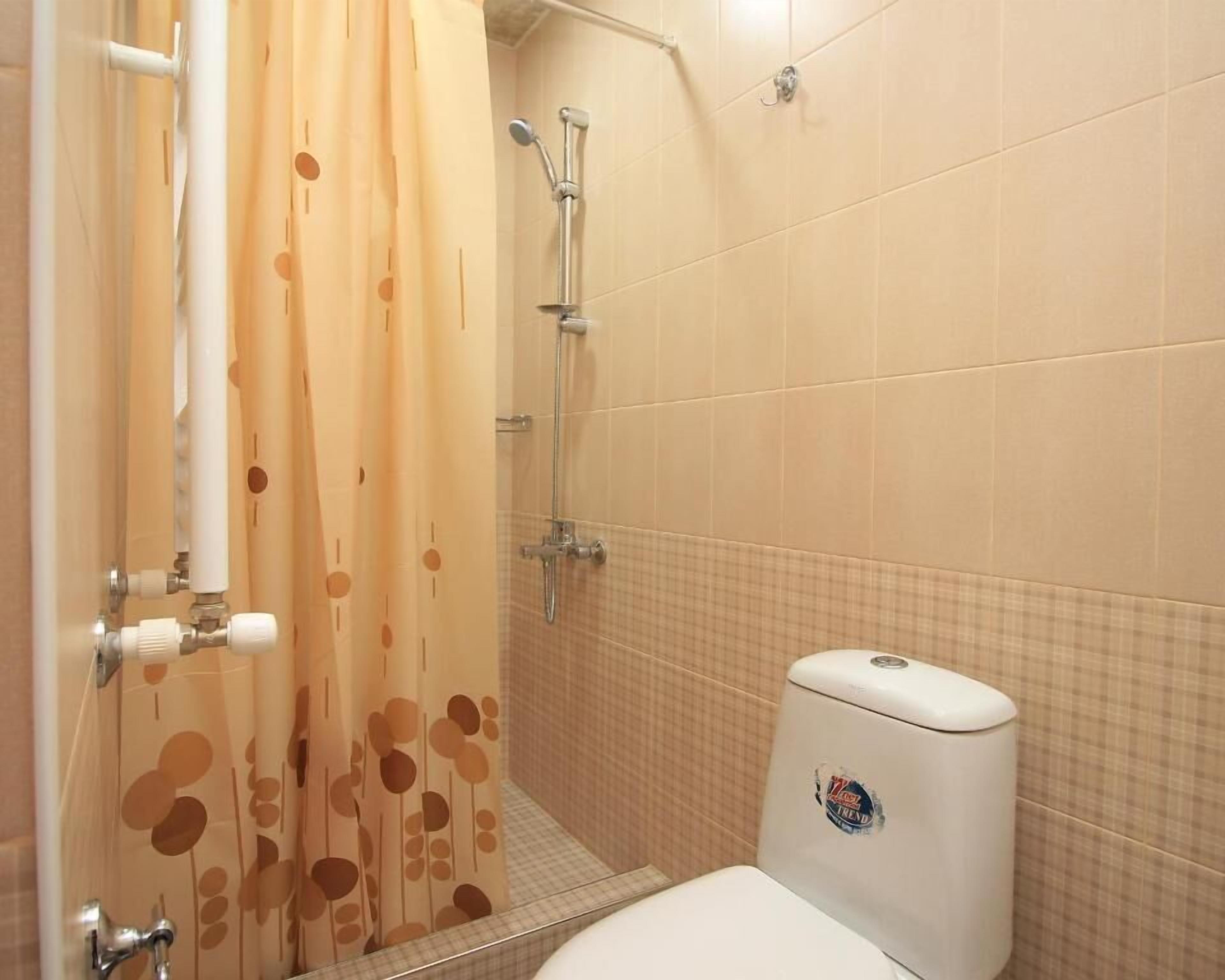 Casa de banho com chuveiro, sanita e cortina com padrão de folhas.